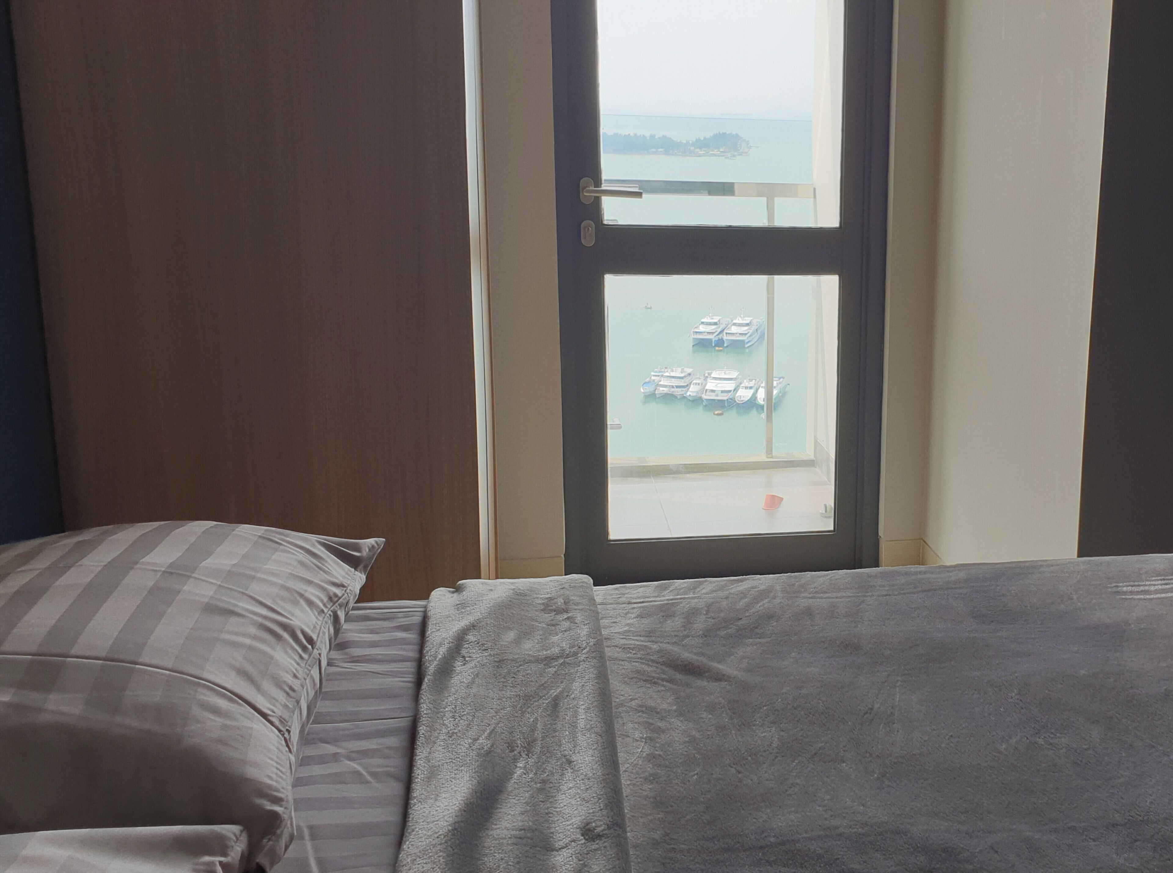 Quarto de hotel com cama, janela e vista para barcos ao longe.