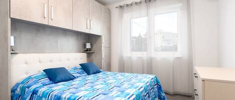 Quarto com cama, guarda-roupa, janela com cortinas e aparelho de ar condicionado.