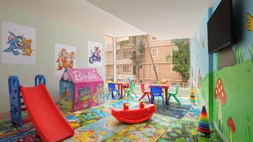 Uma área de recreação infantil com um escorrega, tapetes de jogos coloridos e uma estação de jogos com tema Barbie.
