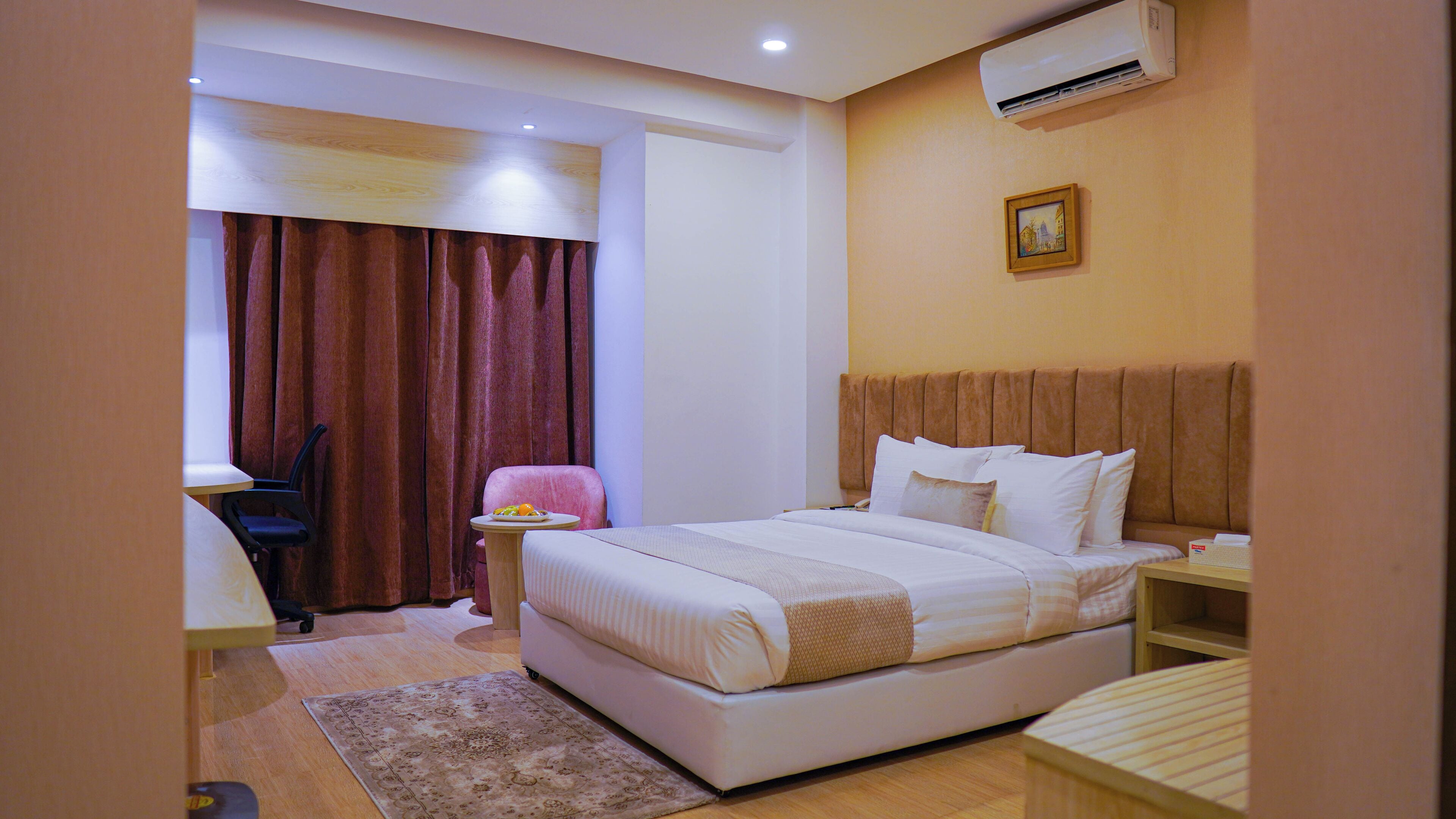 Quarto de hotel com cama, escrivaninha, cadeira e ar condicionado.