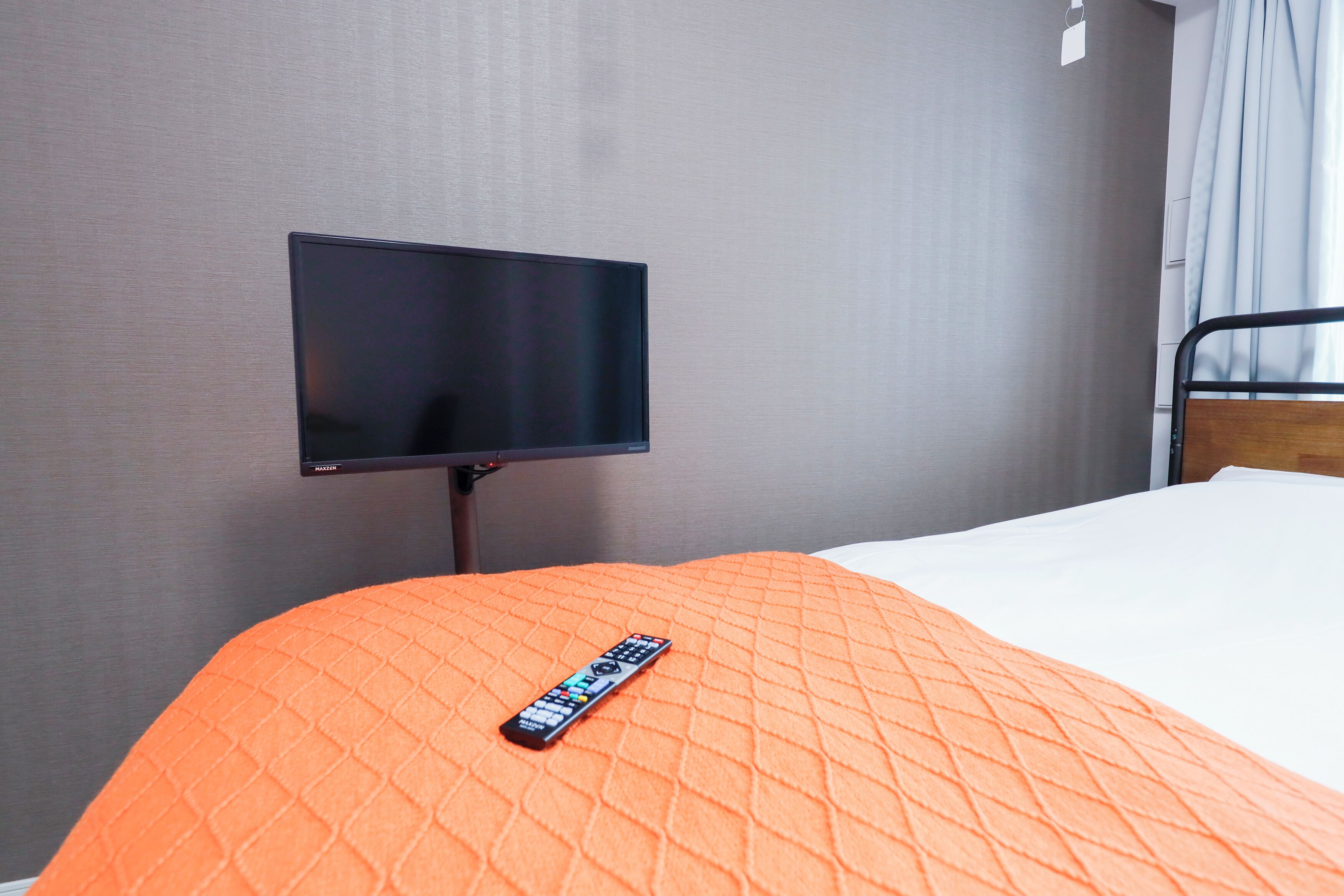 Quarto de hotel com uma cama, um edredom acolchoado laranja, um controle remoto e uma TV de tela plana fixada na parede.