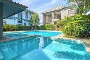 Piscina com borda azulejada, rodeada por vegetação e edifícios.