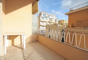 Uma varanda com mesa e grade brancas, com vista para uma área residencial com edifícios altos.