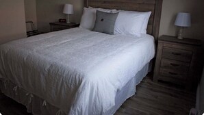 Uma cama grande com cabeceira de madeira, duas mesas de cabeceira com abajures e uma paleta de cores neutras.