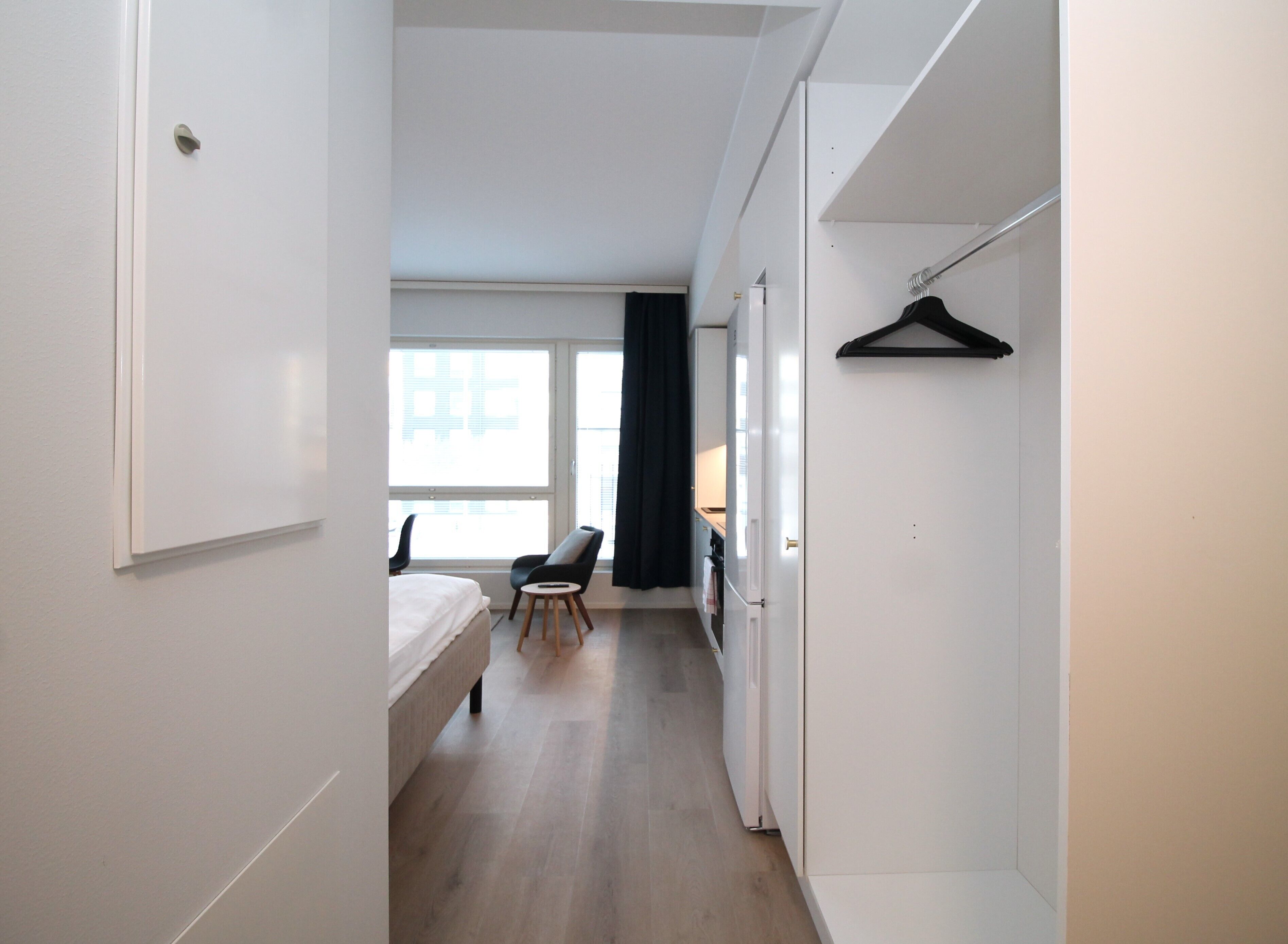 Quarto de hotel moderno com cama, um pequeno espaço de estar, guarda-roupa e janela com cortinas.