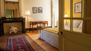 Quarto de hotel com cama, escrivaninha, cadeira, lareira e um espelho grande.