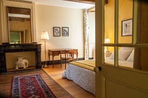 Quarto de hotel com cama, escrivaninha, cadeira, lareira e um espelho grande.