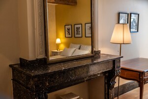 Um aparador de mármore com um espelho refletindo uma cama e um abajur.