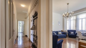 Um corredor com piso lustroso que leva a uma sala de estar com móveis estofados em azul e um candelabro.