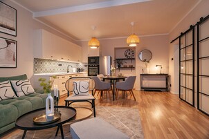 Uma sala de estar moderna com sofá, mesa de centro e cadeiras. Há também uma área de cozinha com armários e uma mesa de jantar.