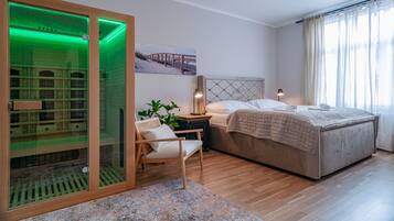 Quarto com cama, cadeira, mesa de cabeceira, luminária, pintura e janela com cortinas.