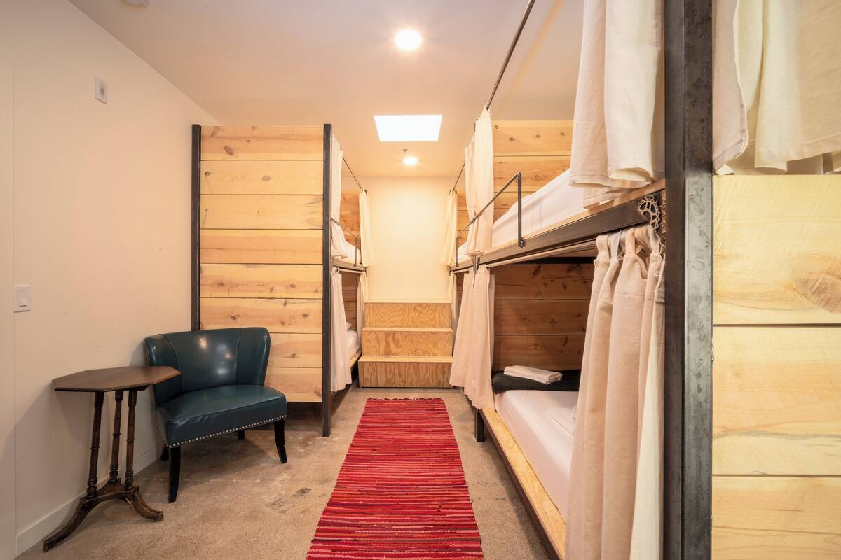 Quarto com beliches, uma mesa pequena, uma cadeira e um tapete vermelho.