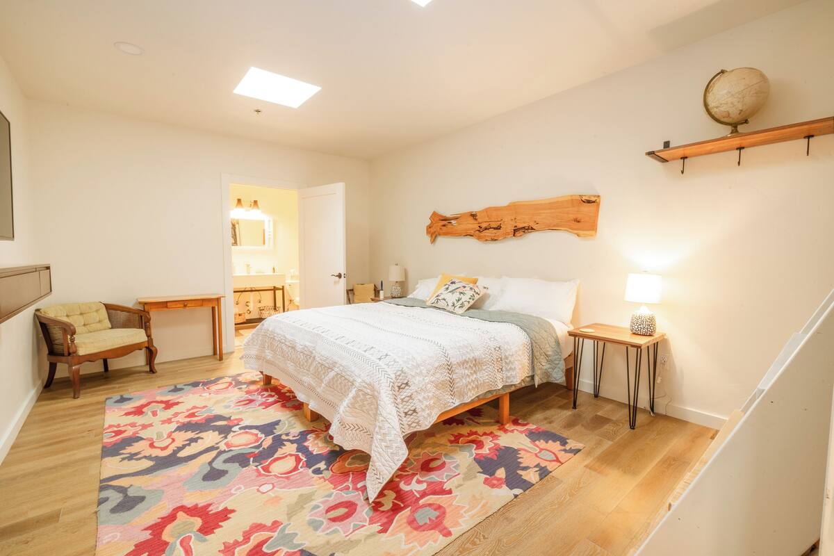 Um quarto com cama, uma cadeira, uma mesinha, um abajur e uma estante com um globo.