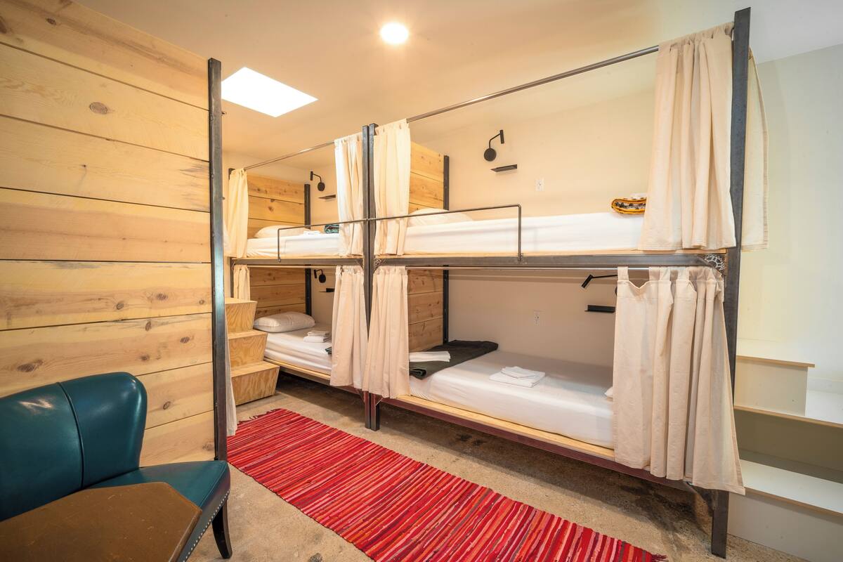 Quarto com beliches, paredes de madeira, tapete listrado vermelho e cadeira azul.
