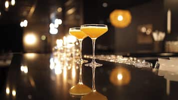 Duas taças de martini com bebida amarelada sobre uma superfície de bar refletora.