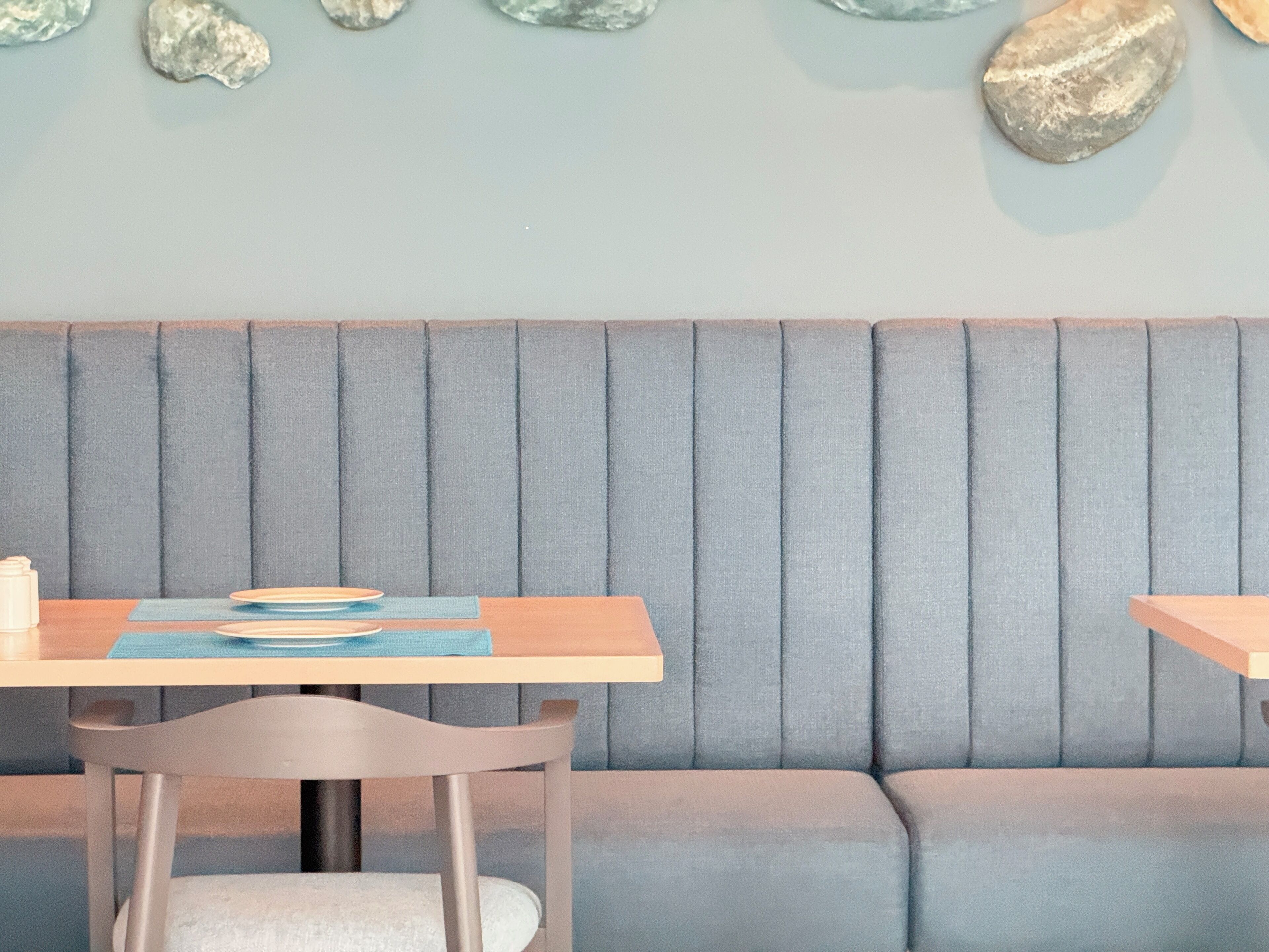 Interior de restaurante com assento acolchoado azul, mesa de madeira com pratos e menu, e cadeira de metal.