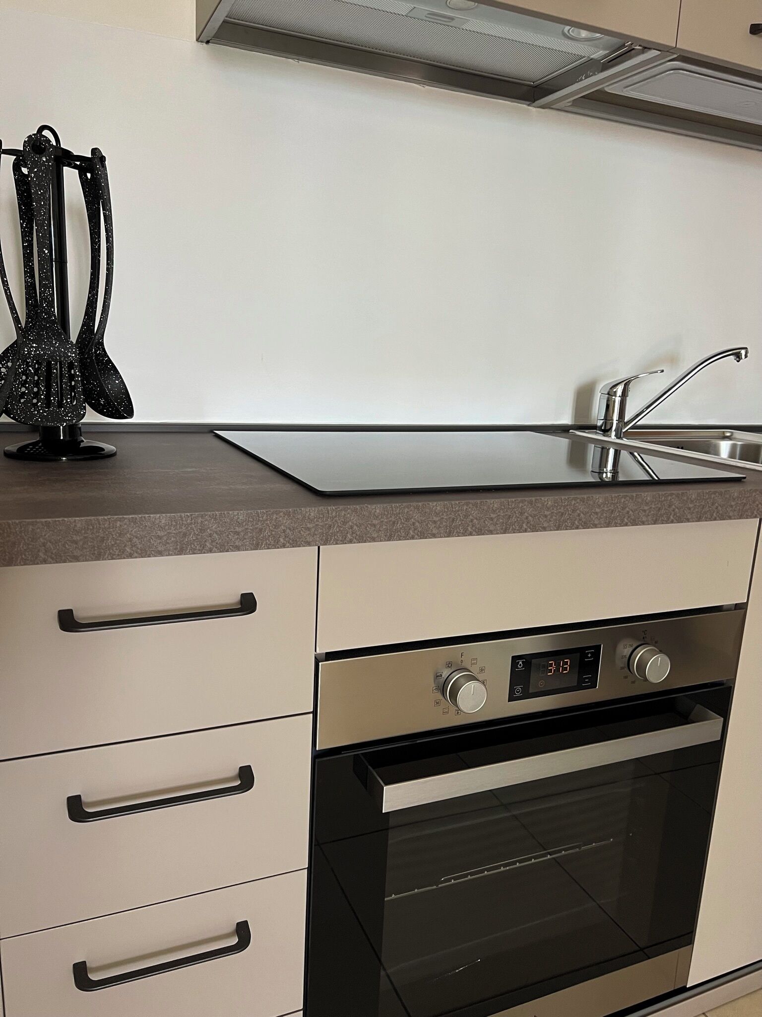 Cozinha com forno de aço inoxidável, relógio digital e pia.
