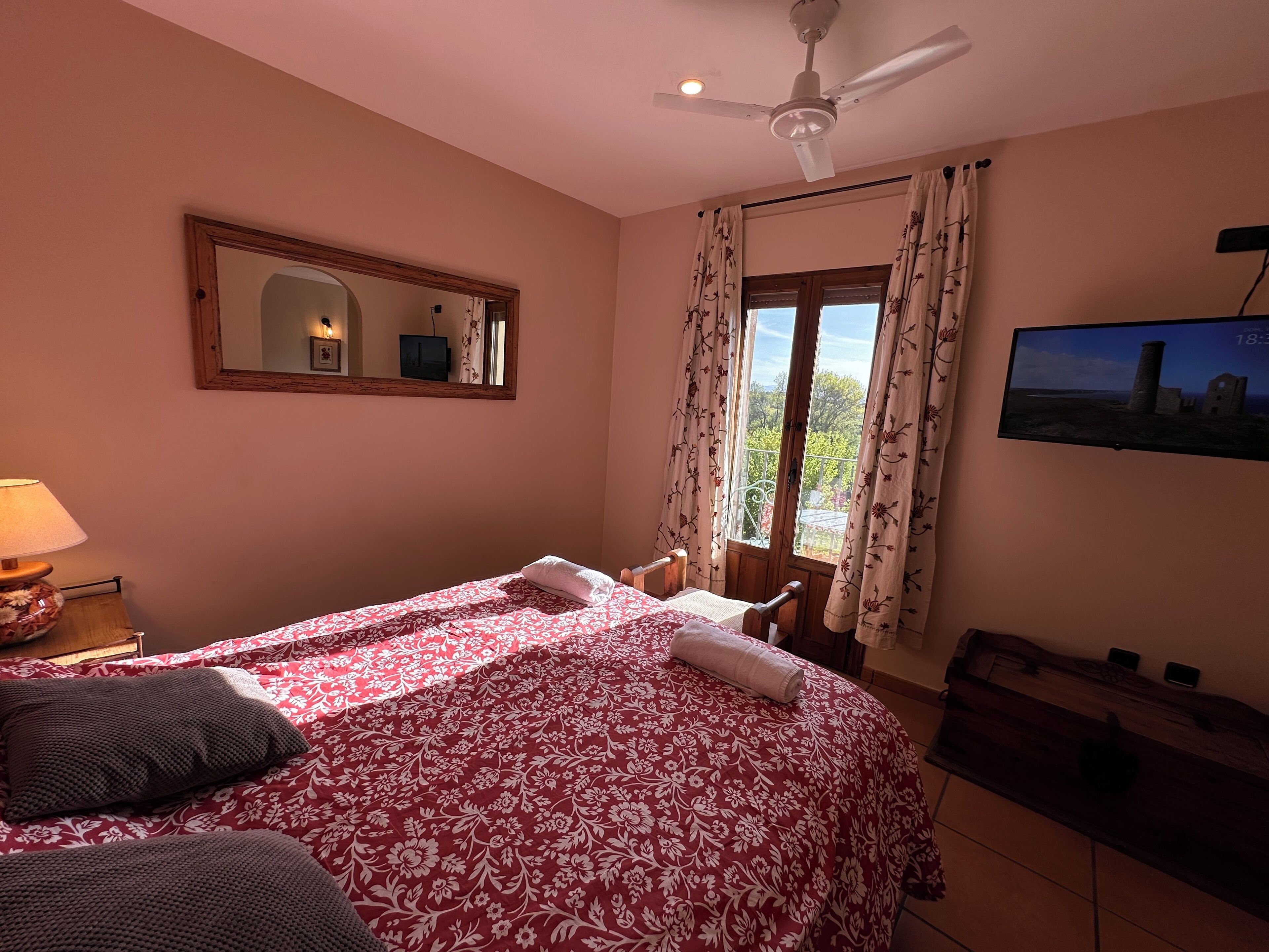 Quarto com duas camas, ventilador de teto, televisão e janela com cortinas.