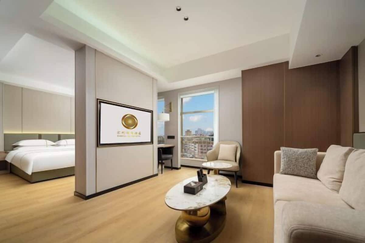 Quarto de hotel moderno com cama, escrivaninha, cadeira, sofá e uma grande janela com vista para a cidade.