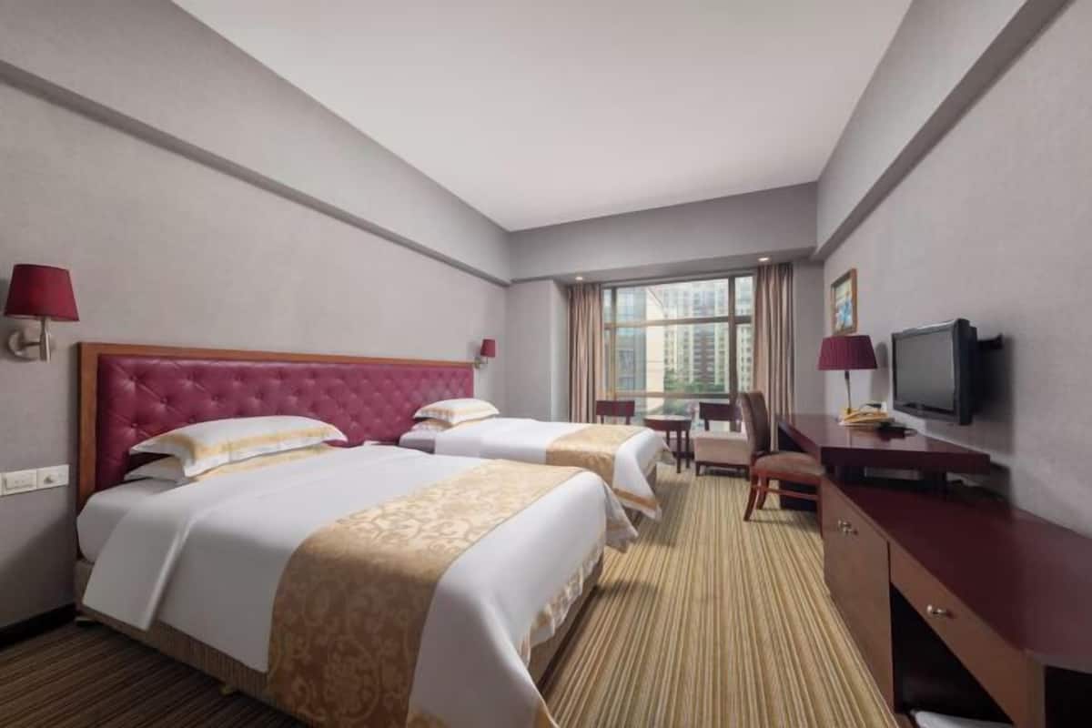 Quarto de hotel com duas camas, uma mesa, uma cadeira, uma televisão e janela com vista para a cidade.