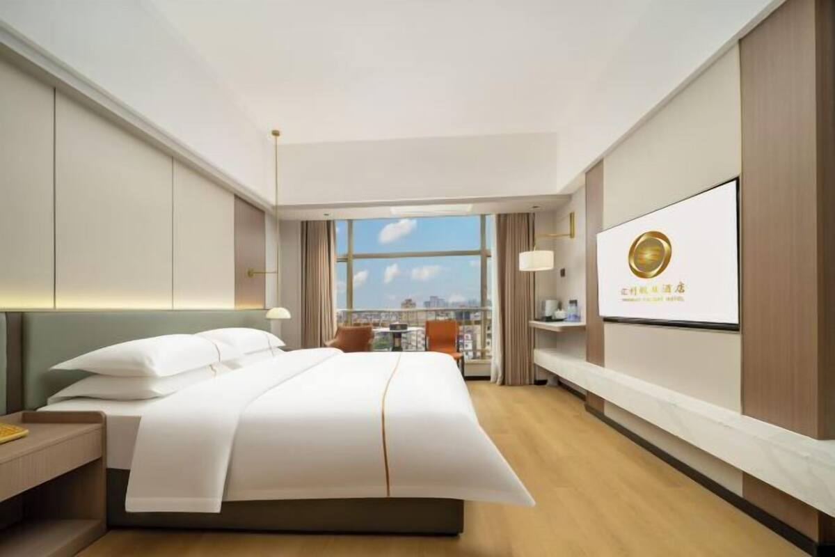 Quarto de hotel moderno com uma cama grande, TV, vista para a cidade e piso de madeira.