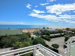Vista de uma praia com céu claro, área de estacionamento e alguma vegetação.
