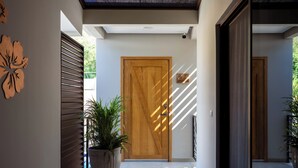 Uma entrada moderna com porta de madeira, um vaso de planta e um objeto decorativo na parede.