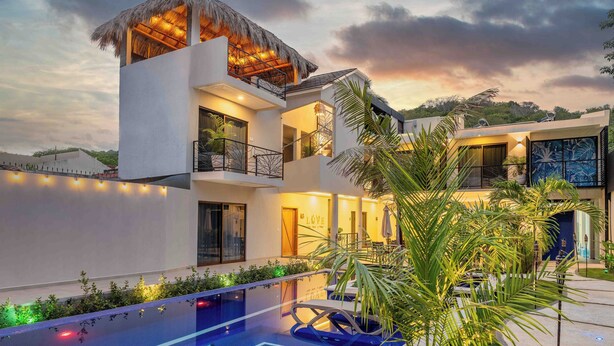 Uma casa moderna de dois andares com piscina, varandas e telhado de palha.