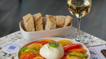 Prato de salada Caprese com tomate, mussarela e manjericão, um copo de vinho branco e uma tigela de pão sobre uma mesa com um cardápio.