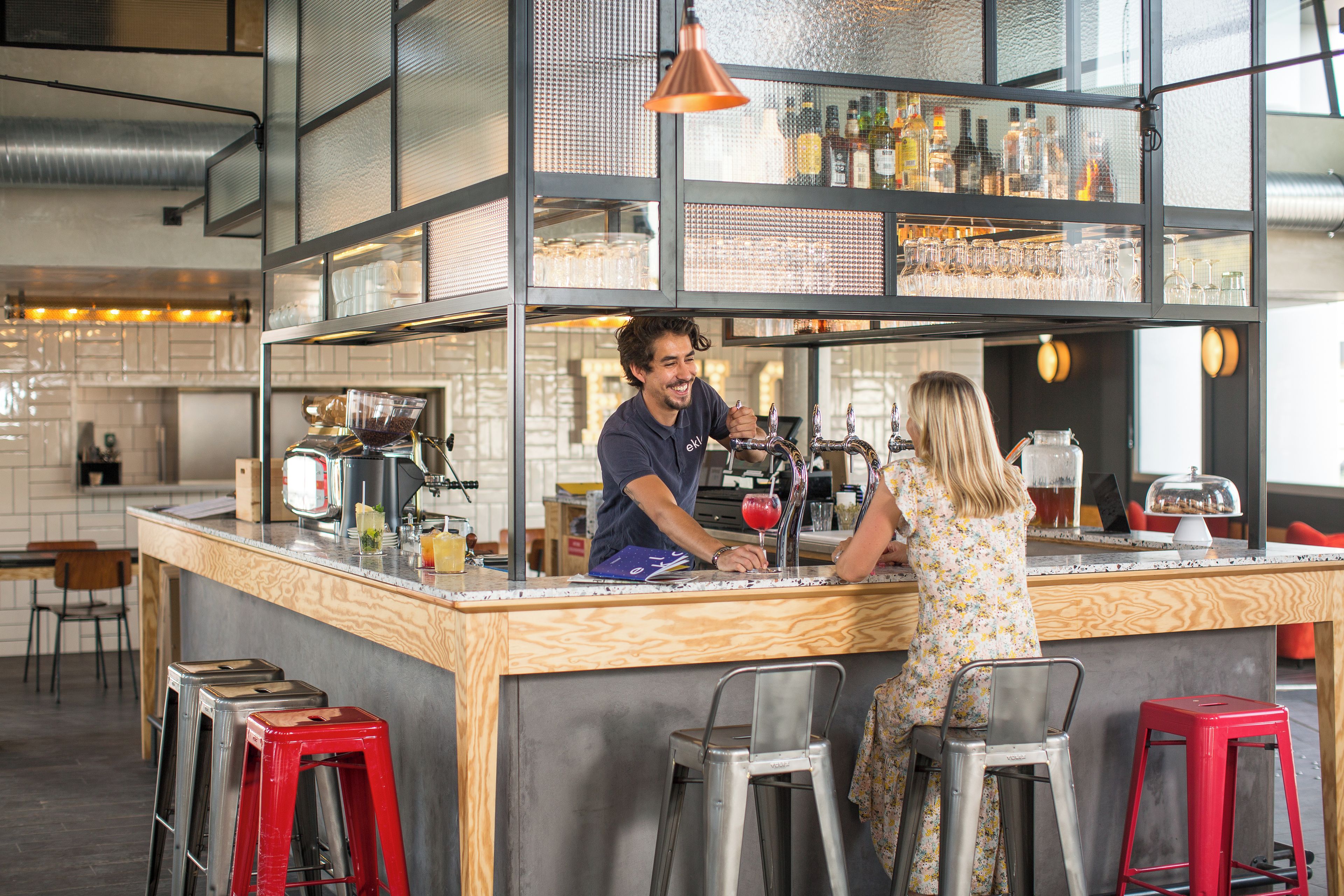 Uma área de bar com banquetas, balcão e um bartender.
