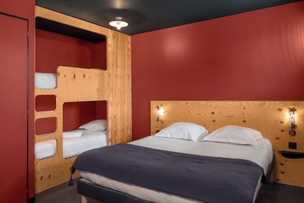 Quarto com beliche, cabeceira de madeira com iluminação e parede vermelha.
