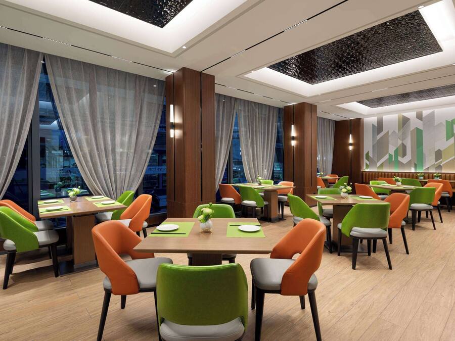 Uma sala de jantar moderna com várias mesas e cadeiras, grandes janelas com cortinas e um design de parede geométrico.