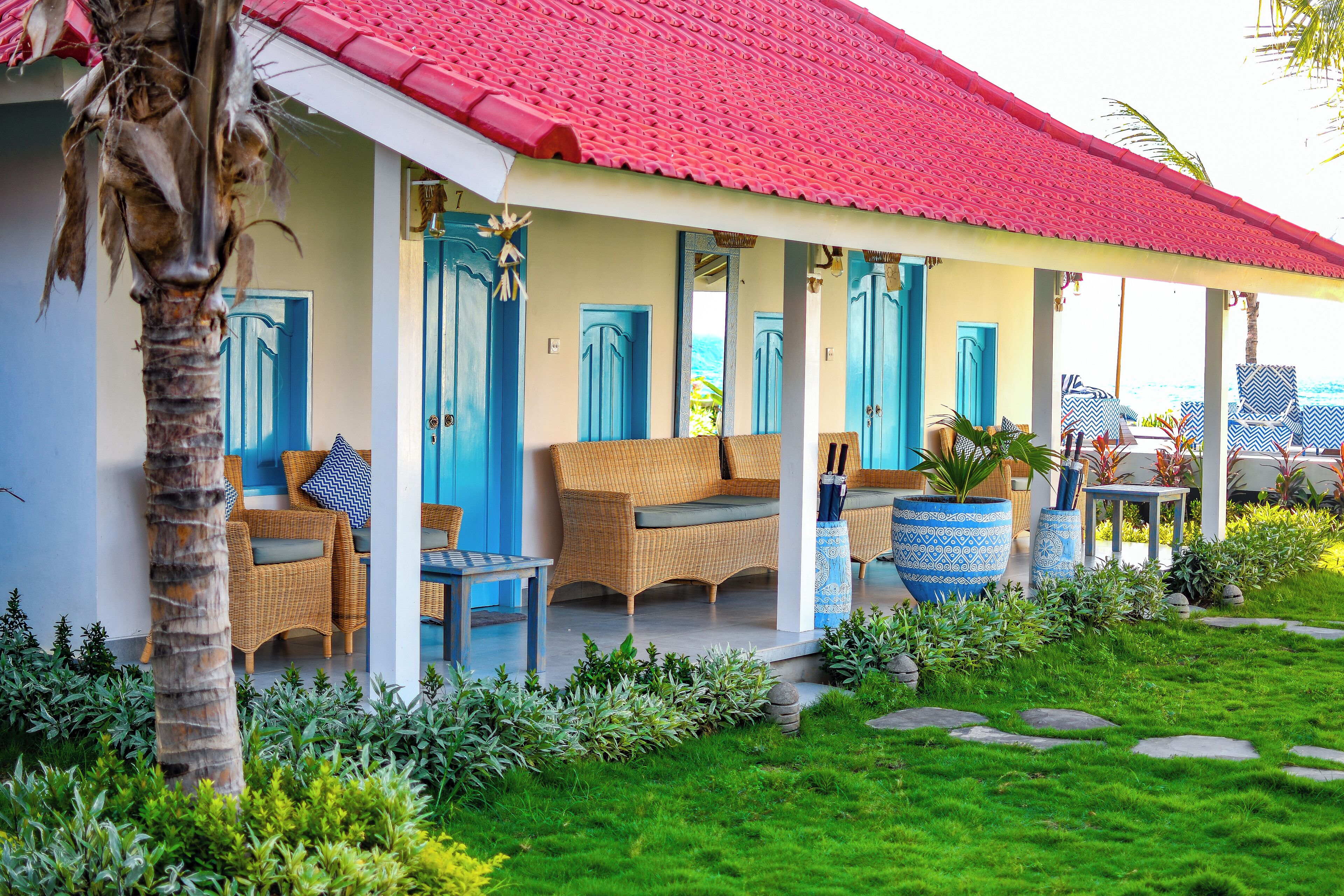 Um resort com telhado vermelho, portas azuis, móveis de vime e um jardim bem cuidado.