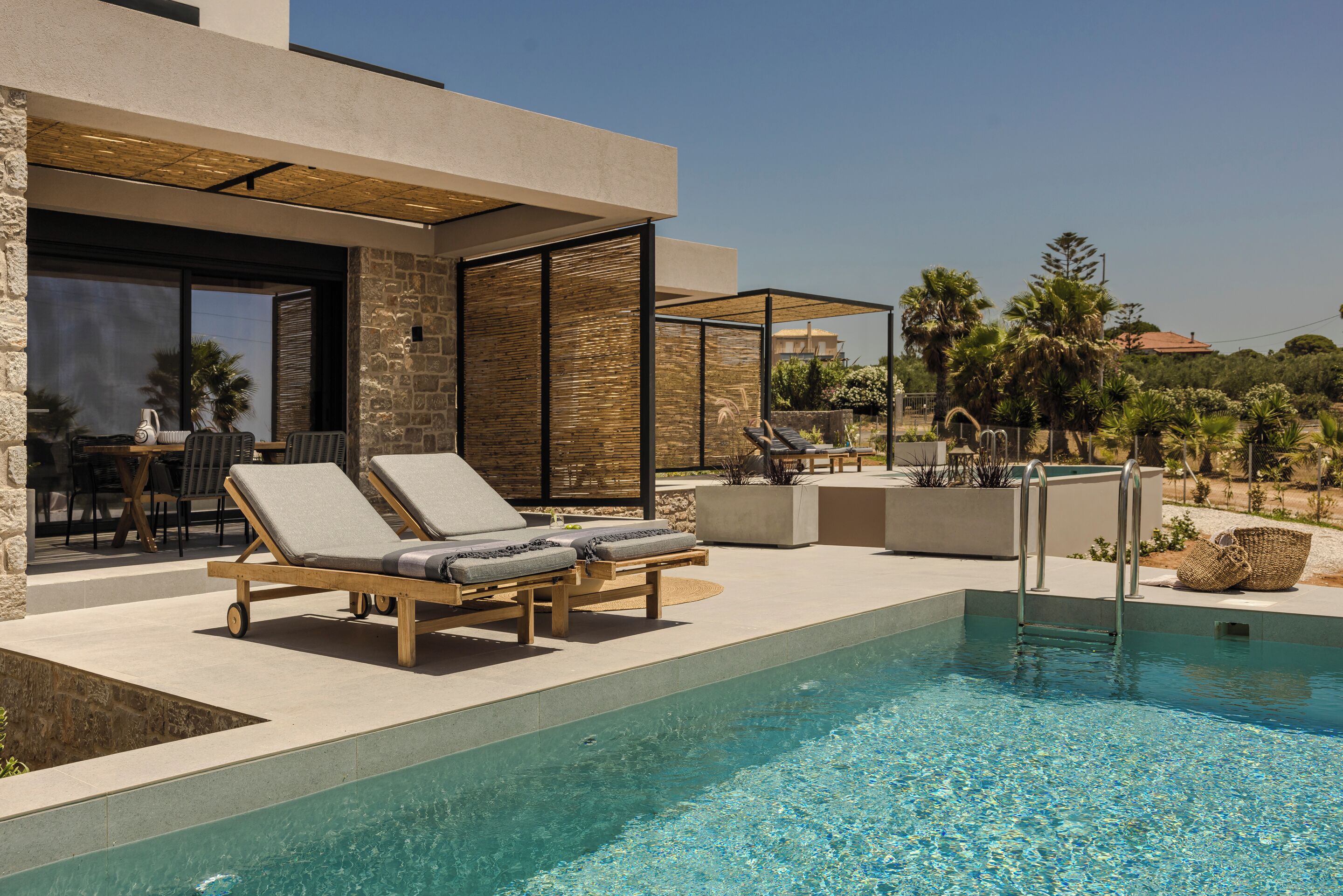 Uma área moderna de piscina ao ar livre, com espreguiçadeiras, piscina e um pátio com mobiliário externo.