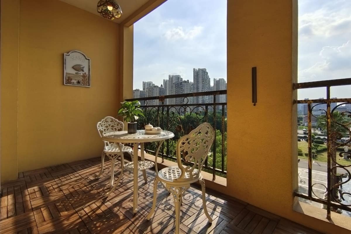 Varanda com vista para edifícios altos, uma mesa redonda pequena com cadeiras e um vaso de planta.