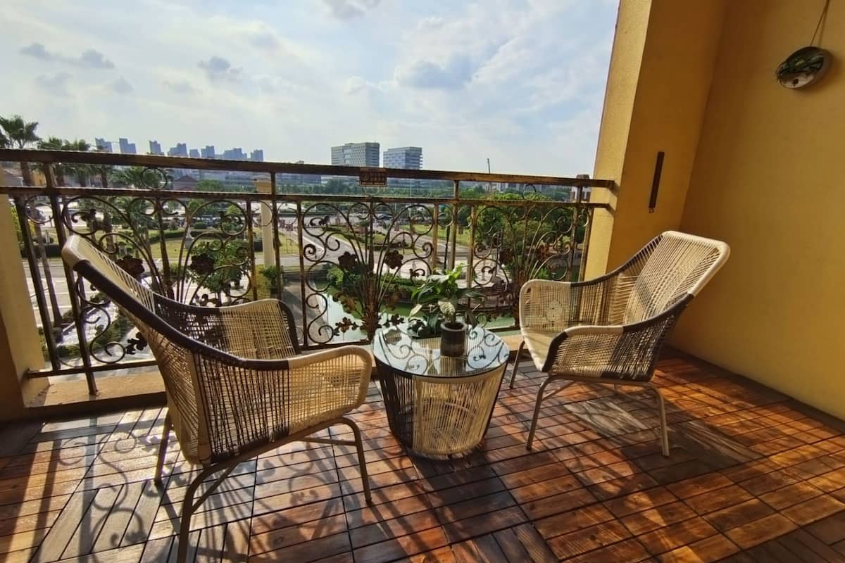 Varanda com cadeiras de vime e mesa de vidro, com vista para uma paisagem urbana com edifícios e vegetação.