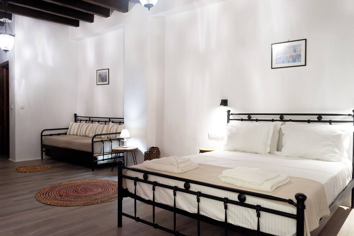 Quarto com uma cama grande, uma cama menor e uma mesa de cabeceira com abajur.