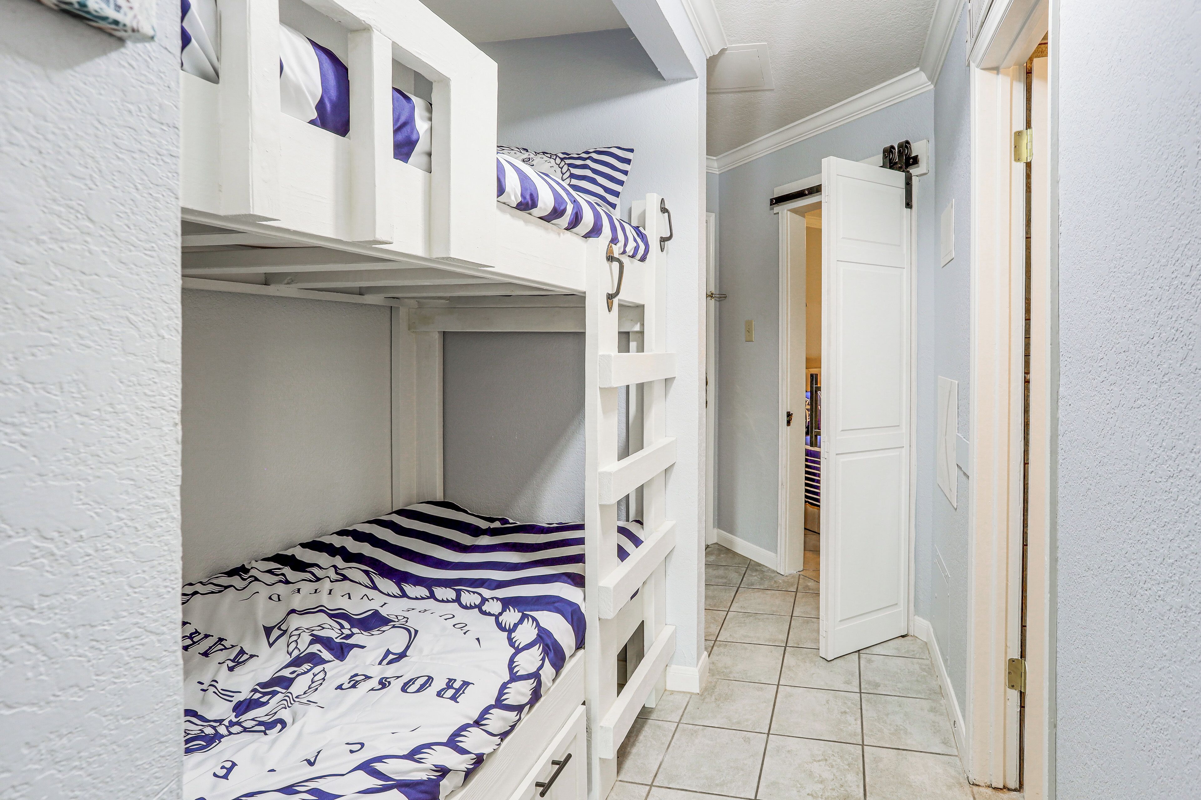 Uma cama beliche com roupa de cama listrada, uma porta branca e um chão de azulejos.