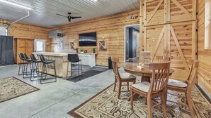 Interior acolhedor de uma cabana, com decoração em madeira, área de cozinha, mesa de jantar com cadeiras e um balcão.