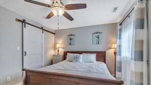 Quarto com cama de madeira, ventilador de teto, duas luminárias e uma porta de correr.