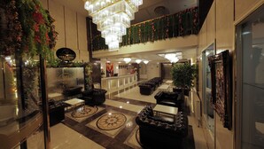 Um hall de hotel com um candelabro, áreas de estar e um balcão de recepção.