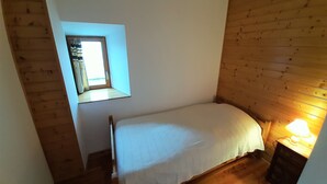 Quarto pequeno com uma cama de solteiro, teto inclinado, janela com vista e abajur.