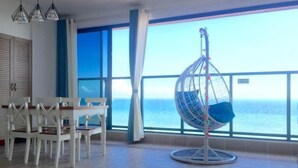 Varanda com cadeira suspensa, mesa de jantar com cadeiras e vista para o mar.