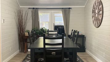 Uma sala de jantar com mesa de madeira, cadeiras, ventilador de teto e um relógio de parede grande.