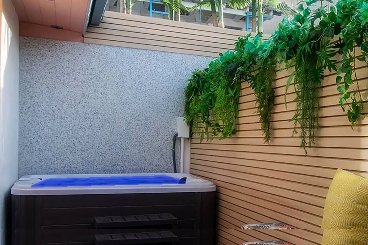 Uma área de spa com hidromassagem, parede texturizada e painel de madeira com plantas verdes.