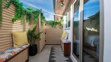 Uma área externa moderna com bancos de madeira, uma planta em vaso e uma porta de vidro que dá para um quarto.