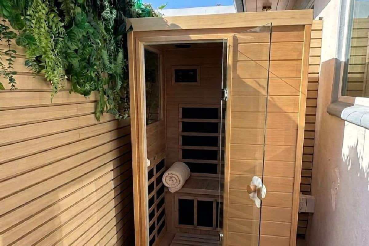 Uma sauna de madeira com porta de vidro, uma toalha e um banco de madeira.