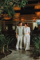 Um casal está em um espaço interno bem iluminado, com luminárias pendentes e plantas em vasos.