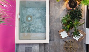 Uma área de spa com banheira de hidromassagem, plantas em vasos e uma cadeira de vime.