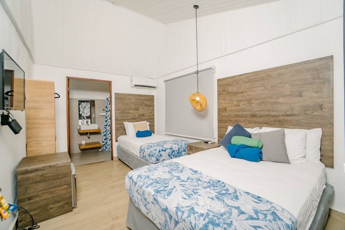 Quarto de hotel moderno com duas camas, cabeceira de madeira, um espelho grande e piso de madeira.